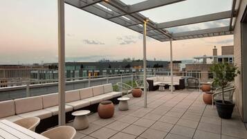 Terraço no telhado com área de estar, plantas em vasos e vista para a paisagem urbana.