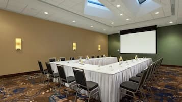 Sala de conferências com uma mesa comprida, cadeiras, tela de projetor e piso coberto de carpete.