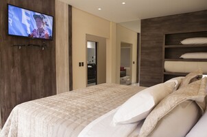 Quarto moderno com uma cama grande, televisão na parede e estante embutida.