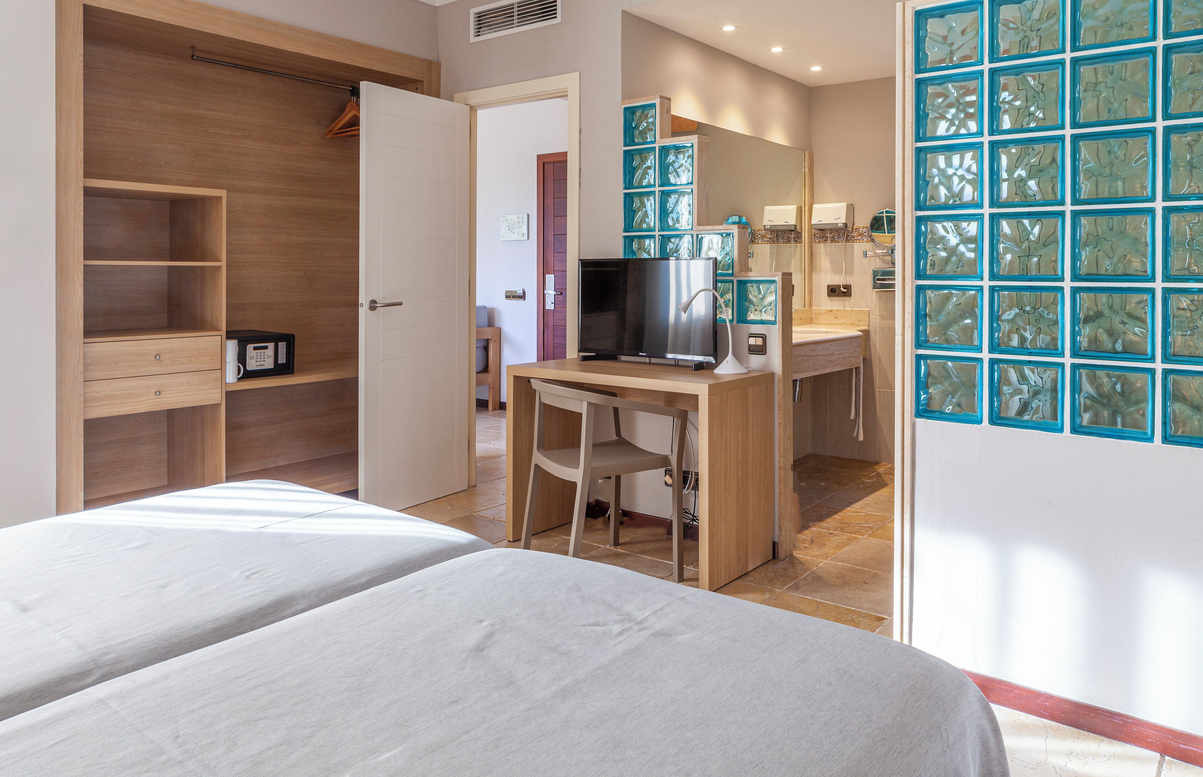 Quarto de hotel com uma cama, uma escrivaninha com cadeira, televisão e guarda-roupa.