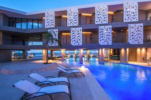 Um hotel com vários andares, piscina, espreguiçadeiras e vista para o mar.