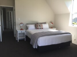 Quarto com uma cama, duas mesas de cabeceira, uma janela e uma porta que dá para outro cômodo.