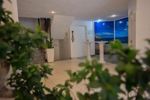 Quarto com vista para o mar, um relógio na parede e escada que leva a outro espaço.