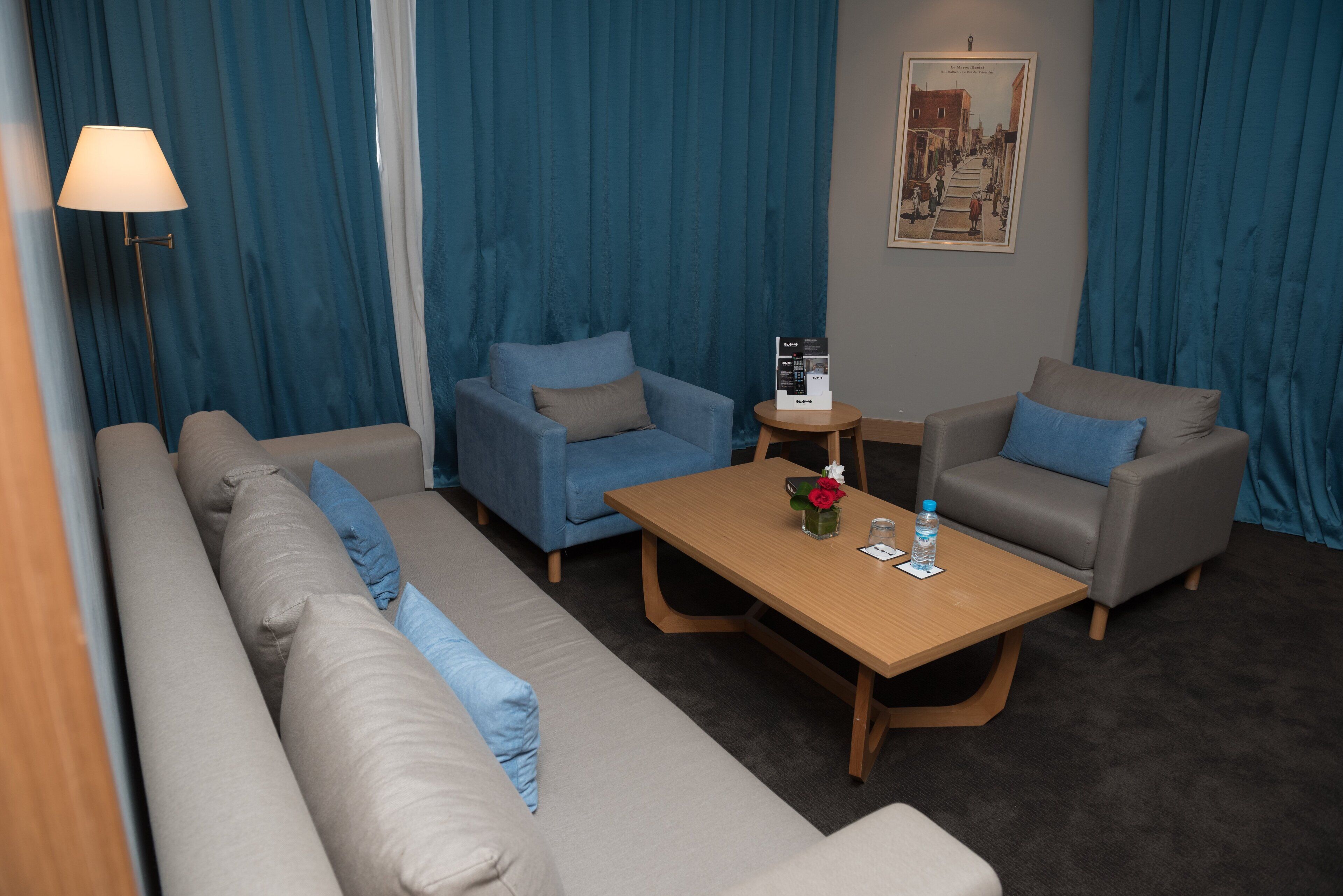 Quarto de hotel moderno com sofá, duas poltronas, uma pequena mesa de madeira, abajur e um quadro na parede.