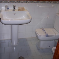 Uma casa de banho com uma pia branca, uma sanita e uma pequena cesta sobre a pia.