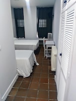 Quarto pequeno com duas camas, uma cadeira e um radiador.