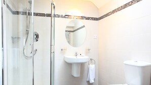 Casa de banho com cabine de duche em vidro, lavatório com espelho e sanita.