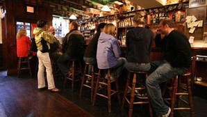 Um bar com banquetas de madeira e prateleiras cheias de garrafas.