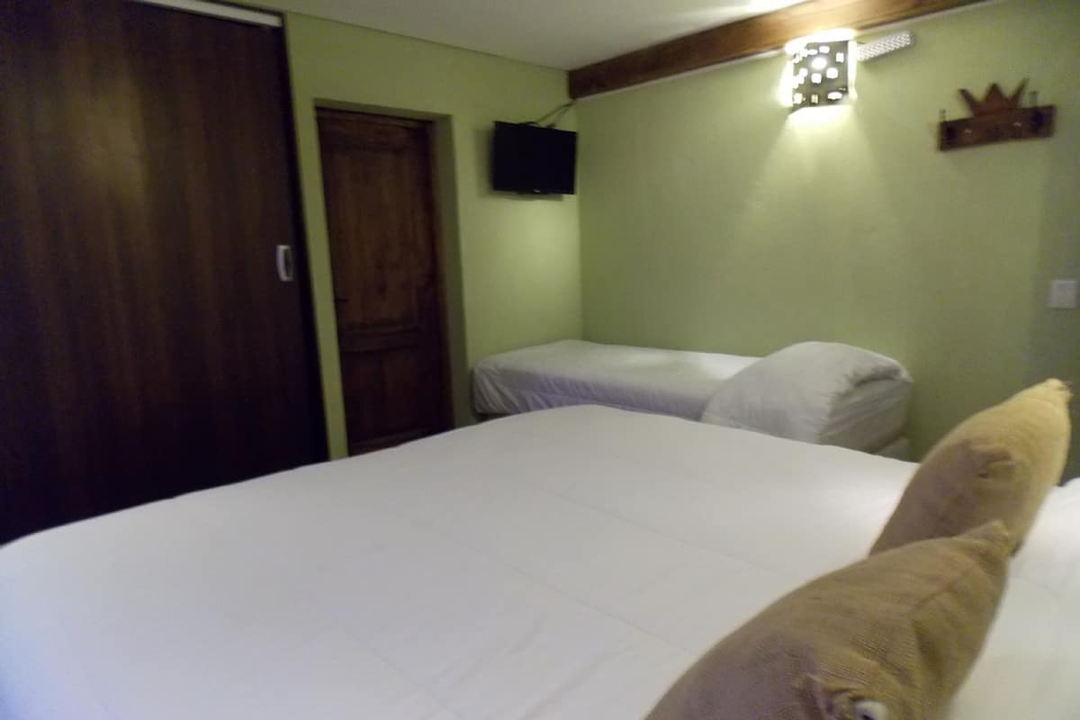 Quarto com duas camas, televisão fixada na parede e porta de madeira.