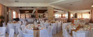 Uma sala de banquetes com mesas redondas preparadas para um evento formal, com toalhas brancas e cadeiras.