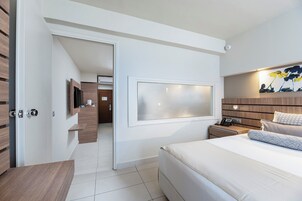 Quarto moderno com uma cama grande, TV montada e mesa de cabeceira com telefone.