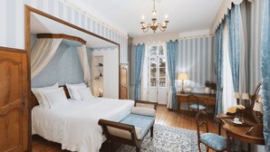 Quarto com cama de dossel, escrivaninha com cadeira e janela com cortinas.