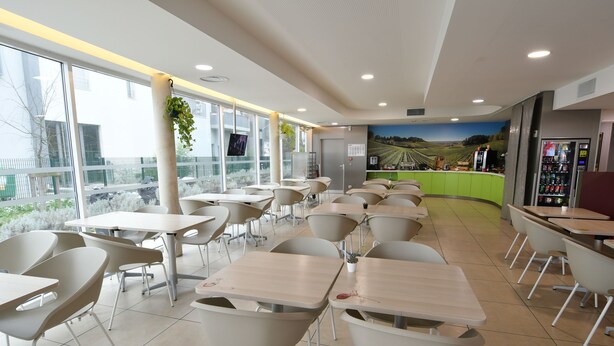 Uma cafeteria moderna com mesas, cadeiras, máquina de vendas automática e um mural na parede.