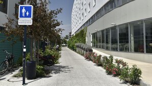 Um edifício moderno com uma passarela para pedestres, uma placa indicando prioridade para ciclistas e uma bicicleta estacionada ao lado.