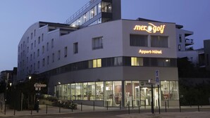 Um hotel moderno com um sinal de 'mergolf' bem visível, uma área de recepção e fachada de vidro.