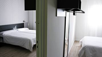 Quarto de hotel com duas camas, um guarda-roupa e uma televisão fixada na parede.