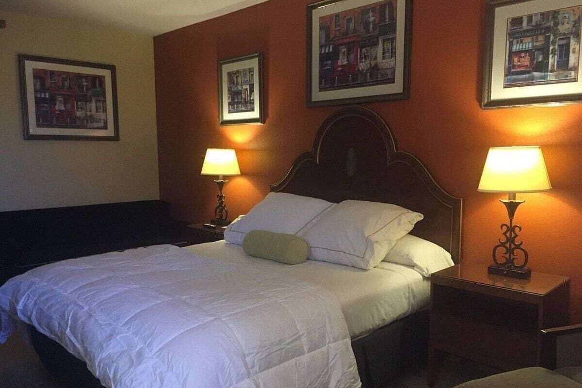 Quarto de hotel com uma cama, duas mesas de cabeceira com luminárias e três quadros na parede.