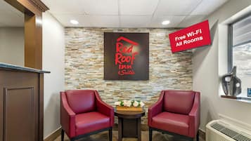Lobby de um hotel Red Roof Suites, com duas poltronas de couro, parede de pedra e sinal indicando Wi-Fi gratuito em todos os quartos.
