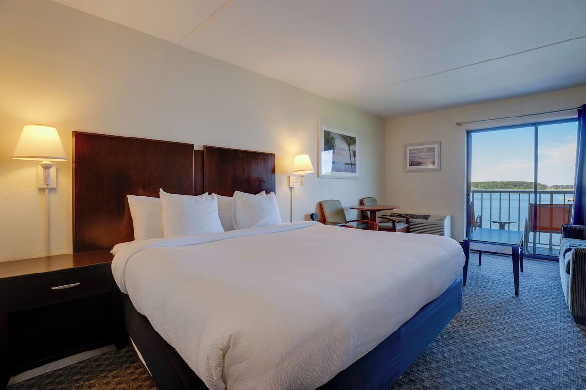Quarto de hotel com uma cama grande, luminárias de cabeceira, uma escrivaninha e varanda com vista.