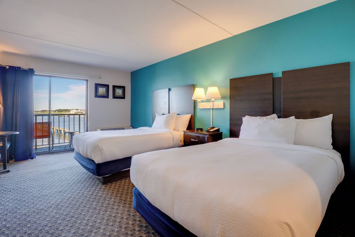 Quarto de hotel com duas camas, varanda e vista para a água.
