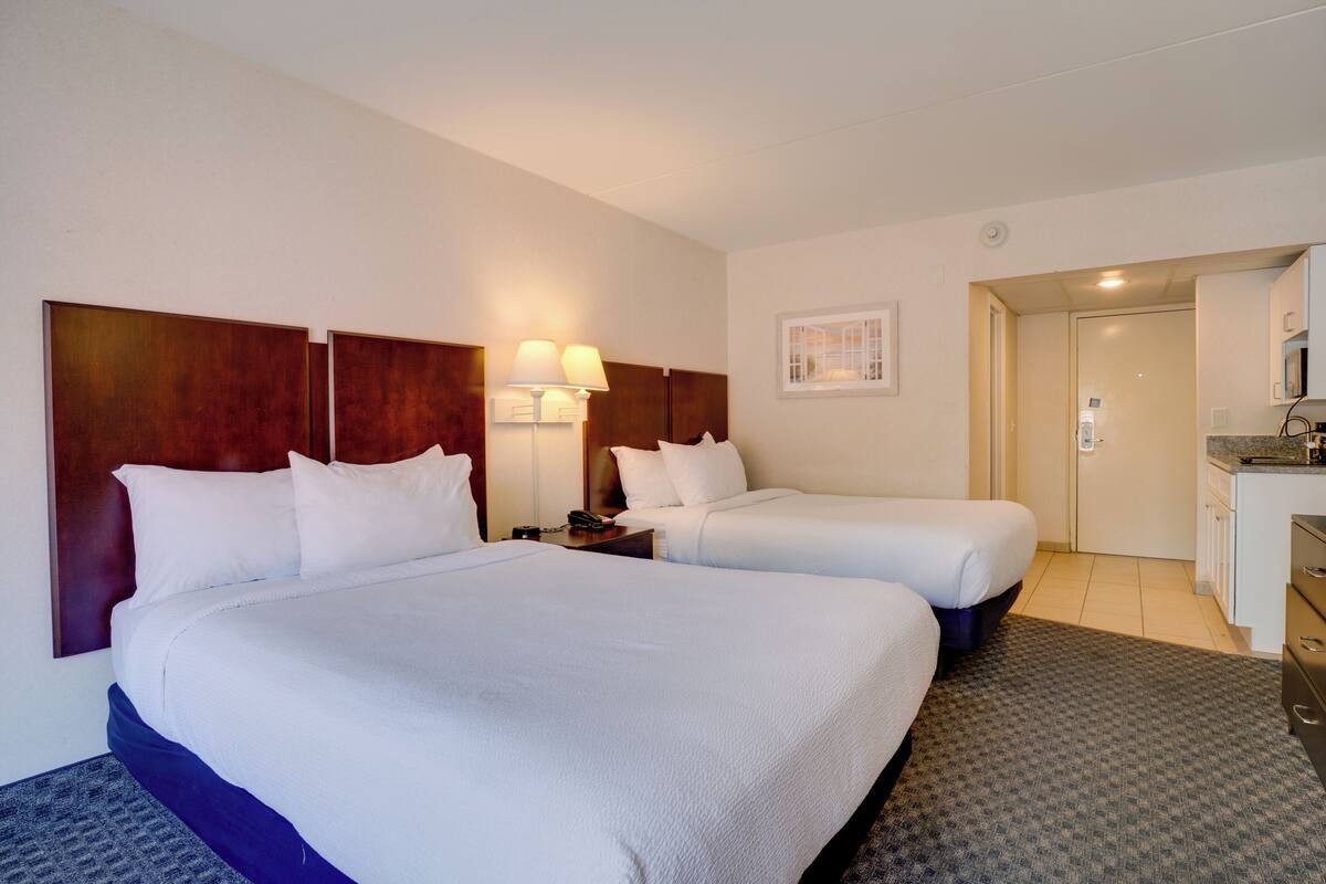 Quarto de hotel com duas camas, uma mesa, uma cadeira e a porta do banheiro.