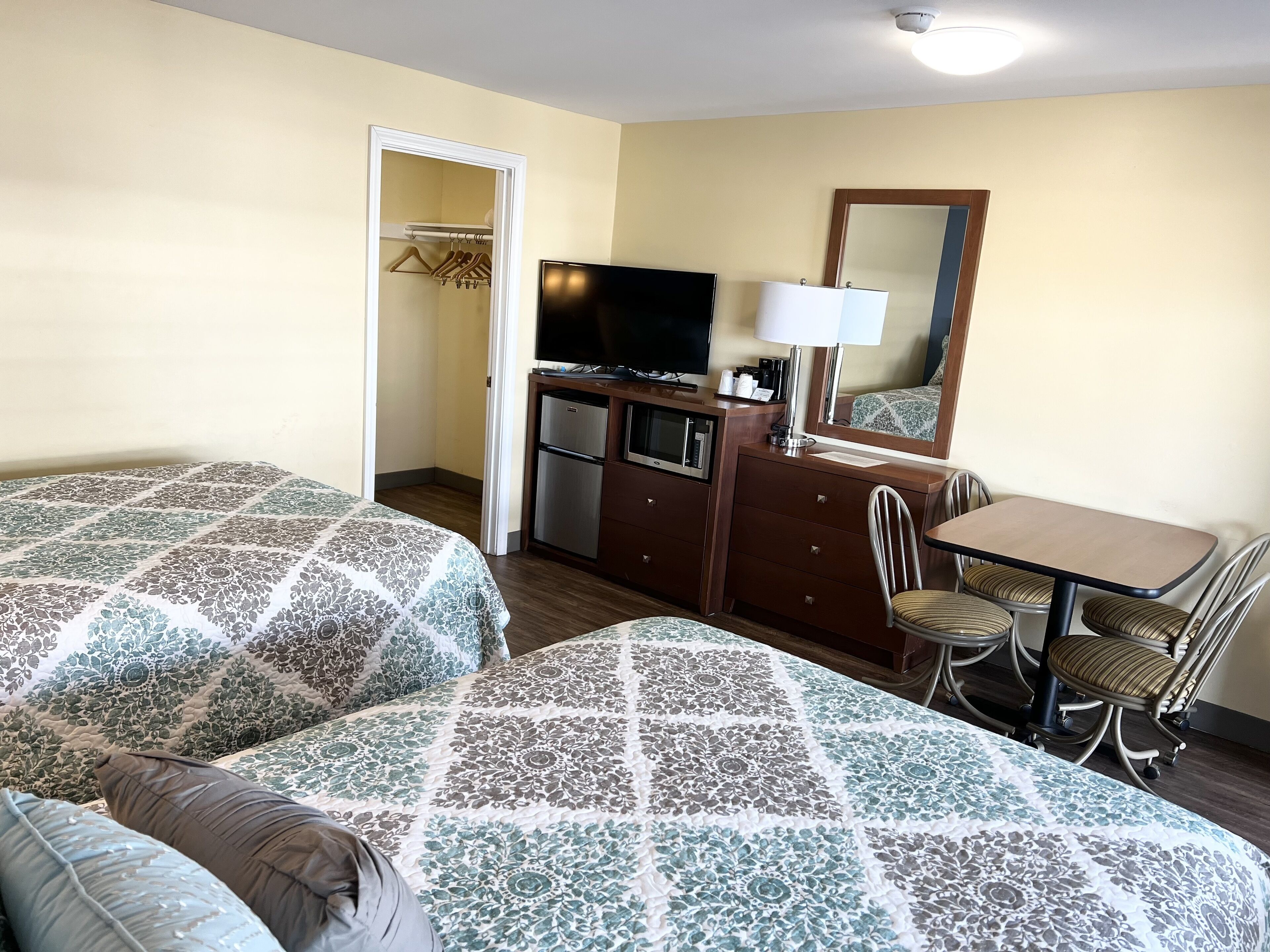 Quarto de hotel com cama, escrivaninha, cadeira, televisão, espelho e guarda-roupa.