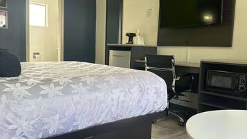 Quarto de hotel com uma cama, uma escrivaninha, uma cadeira, uma televisão e um micro-ondas.