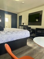 Quarto de hotel com uma cama, uma escrivaninha, uma cadeira, uma televisão e um micro-ondas.