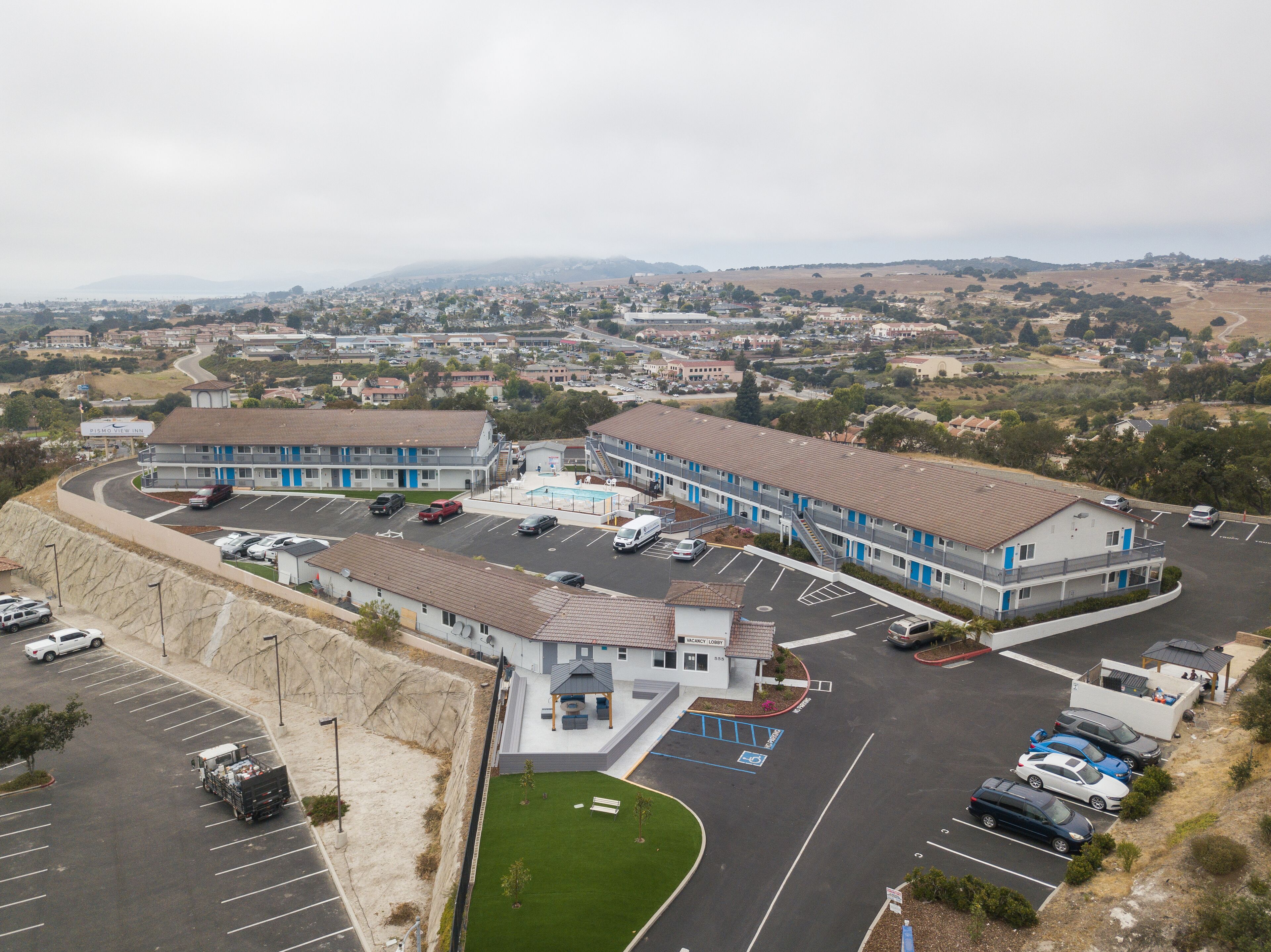 Um motel com estacionamento, piscina e vista para a cidade ao redor.