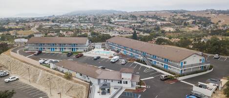 Um motel com estacionamento, piscina e vista para a cidade ao redor.