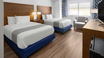 Quarto de hotel com duas camas, uma escrivaninha, uma cadeira, uma televisão e uma janela com vista.