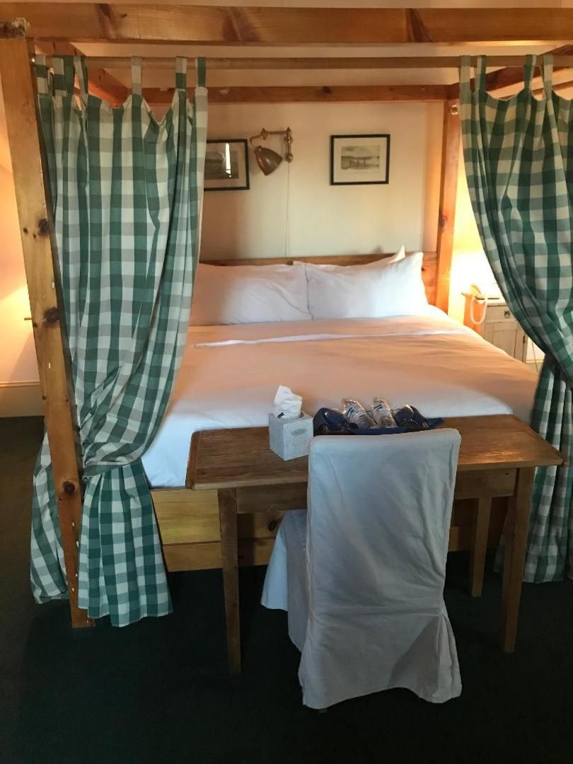 Uma cama com cabeceira de madeira, uma mesinha de cabeceira com um estojo de lenços e um par de sapatos no chão.