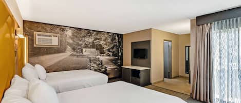 Quarto de hotel com duas camas, televisão de tela plana, uma pequena escrivaninha e uma janela grande com cortinas.
