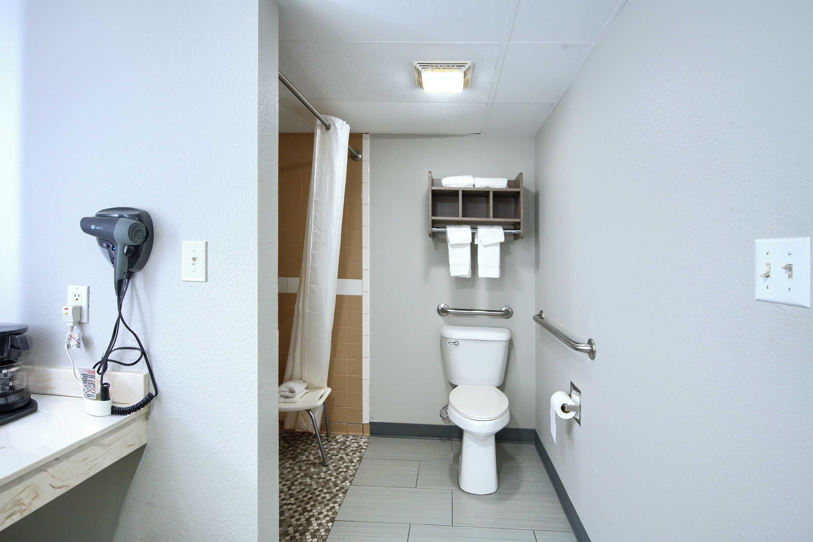 Um banheiro pequeno e limpo, com vaso sanitário, porta-toalhas, cortina de chuveiro e secador de cabelo em uma bancada.