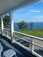 Espaço coberto ao ar livre com vista para o mar, área gramada e cerca branca.