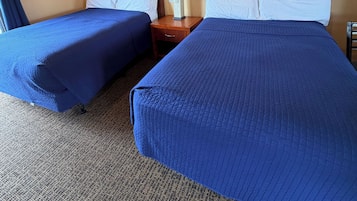 Quarto de hotel com duas camas, teto de madeira, ar condicionado fixado na parede e mesa de cabeceira com abajur.