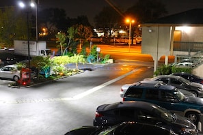 Um estacionamento com vários carros e um caminhão, rodeado por vegetação e iluminado por postes de luz.
