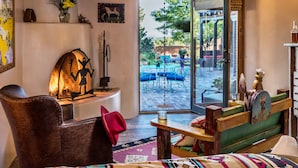 Um quarto acolhedor com lareira, um sofá verde e vista para um pátio ao ar livre com cadeiras azuis e uma mesa.
