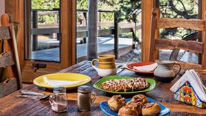 Uma mesa de madeira com itens de café da manhã, vista para um deck e decoração rústica.