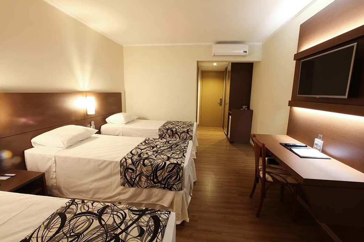 Quarto de hotel com duas camas, uma escrivaninha e uma televisão.