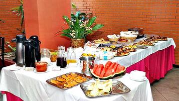 Uma mesa de buffet com diversos alimentos, acompanhamentos e uma planta em vaso.