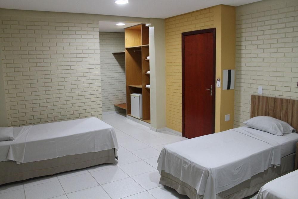 Quarto de hotel com duas camas de solteiro, um guarda-roupa, um espelho e uma porta.