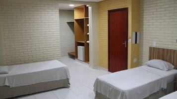Quarto de hotel com duas camas de solteiro, um guarda-roupa, um espelho e uma porta.