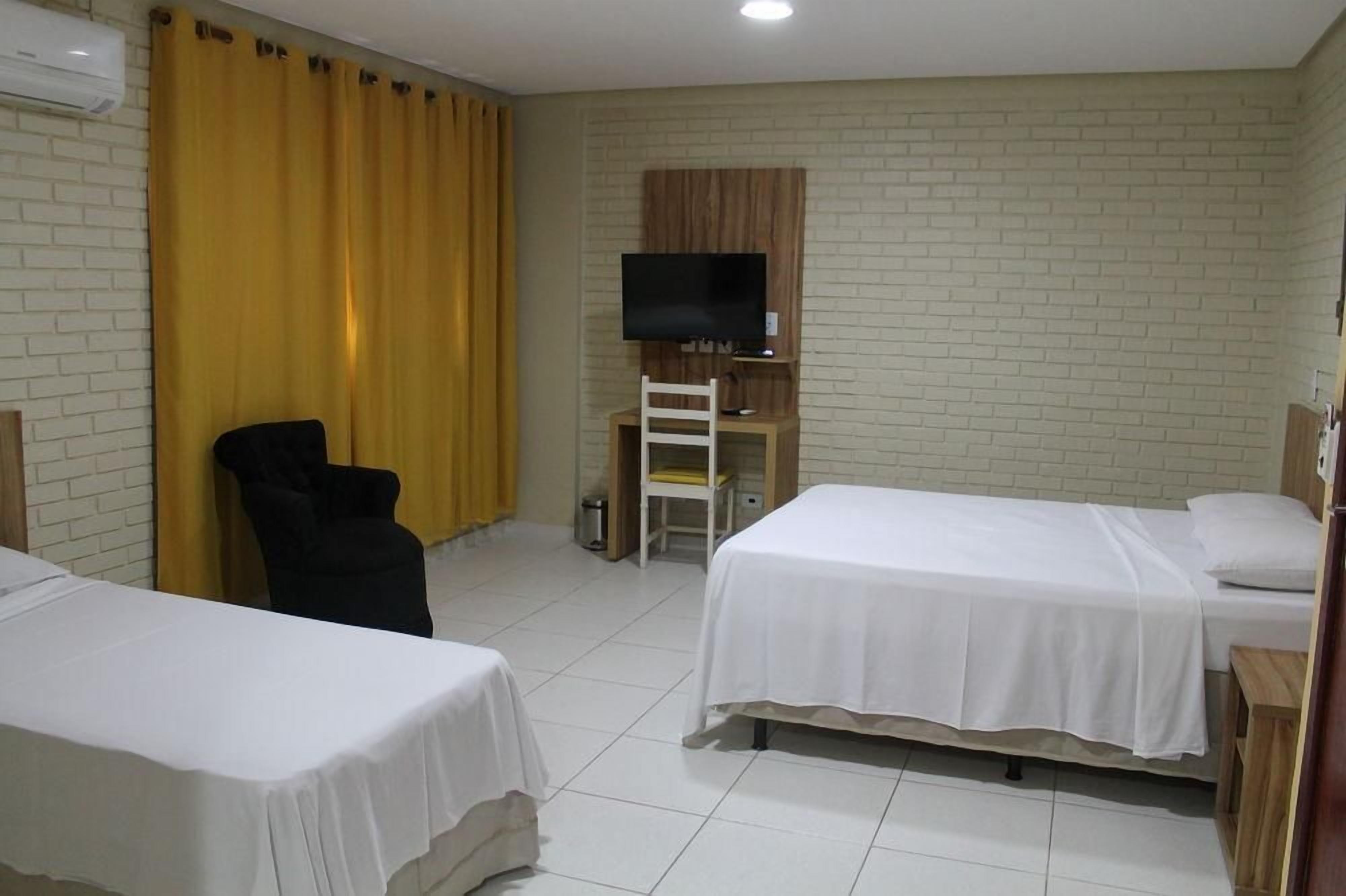 Quarto de hotel com duas camas, uma televisão sobre um suporte de madeira, uma cadeira e uma escrivaninha.