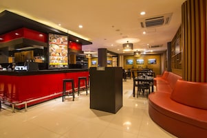 Um restaurante moderno com balcão vermelho, banquetas pretas e uma área de estar com sofá vermelho.