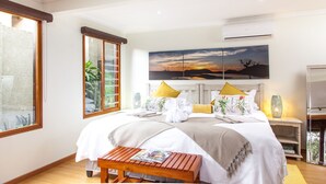 Quarto com cama grande, um banquinho de madeira, mesa de cabeceira e ar condicionado fixado na parede.