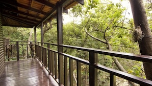 Um deck de madeira com grade de metal que oferece vista para uma área arborizada.