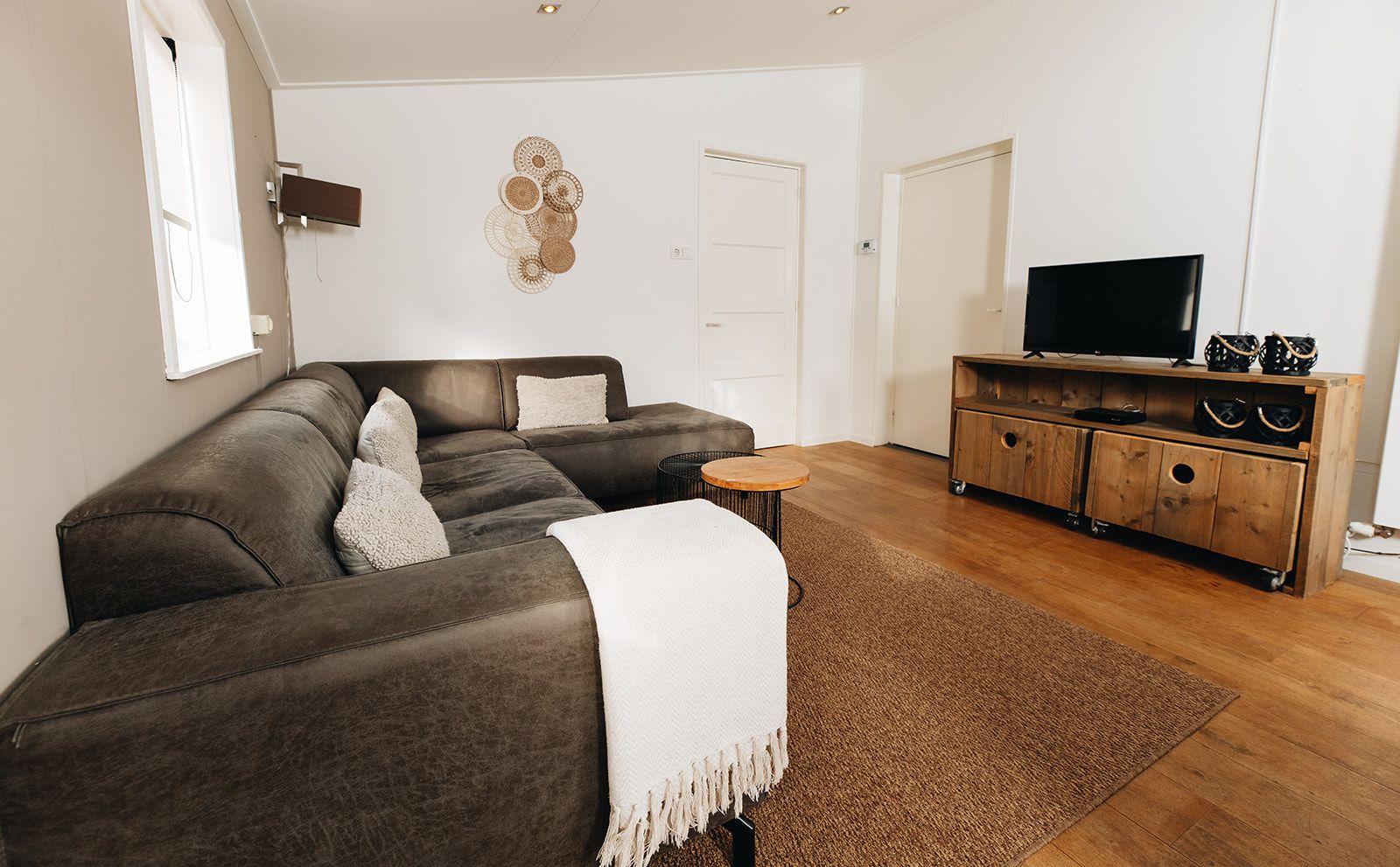 Uma sala de estar moderna com um sofá de couro, uma mesinha redonda, uma TV sobre um suporte de madeira e um objeto decorativo na parede.