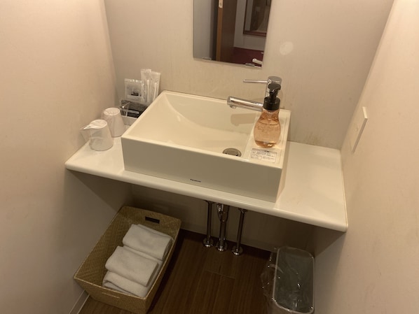 Casa de banho com lavatório branco, espelho em cima e um pequeno contentor de lixo.