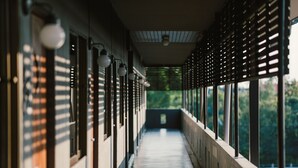Um corredor com piso de azulejos, portas de madeira e vista para o verde lá fora.